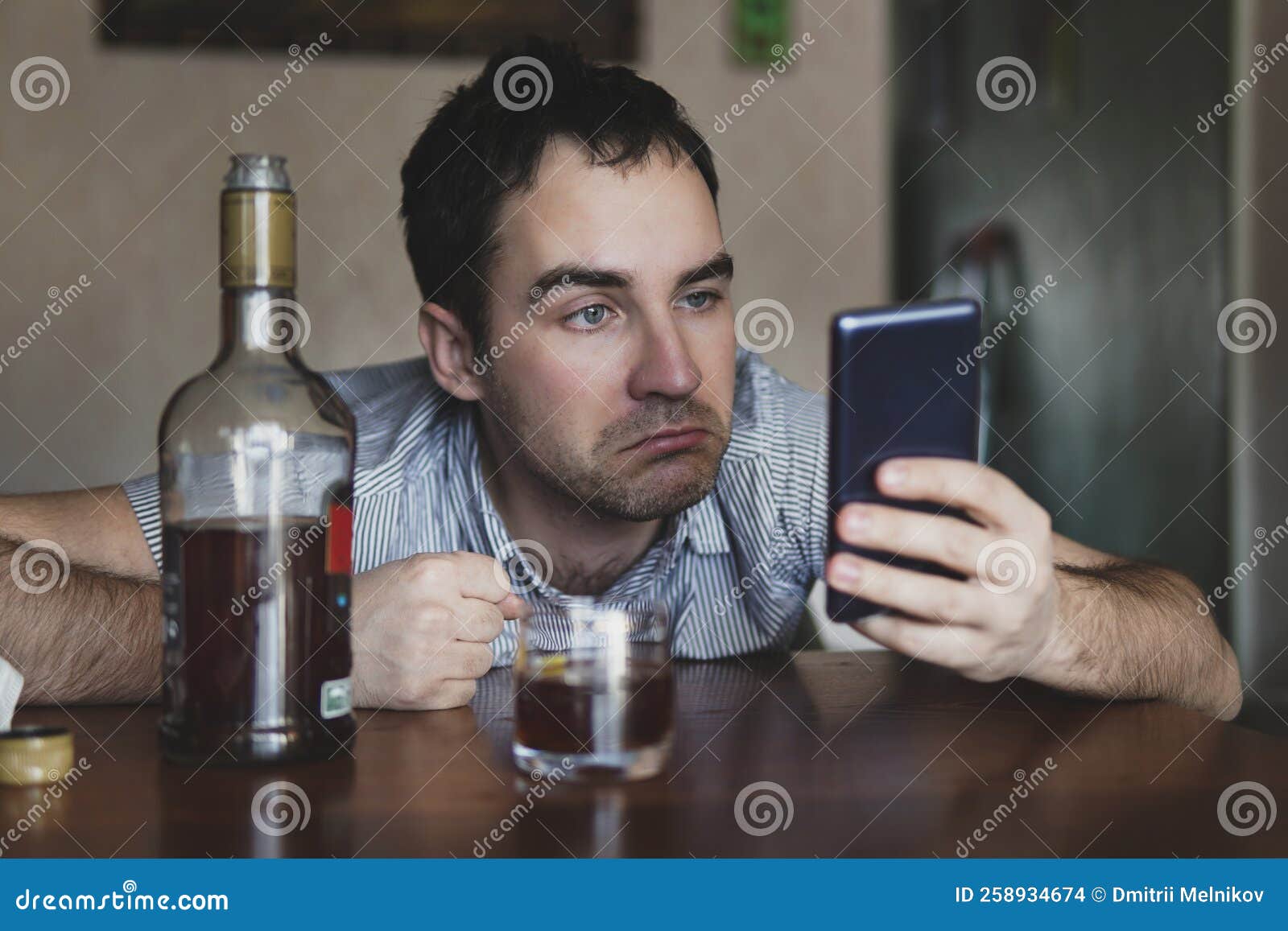 A Drunk Person is Sitting at Table at Home and Reading a Message on a ...