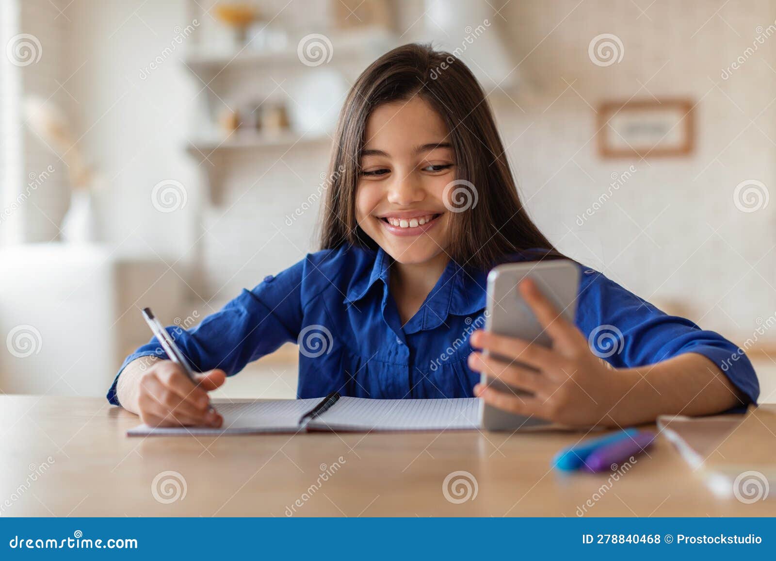 Cheerful Schoolgirl Using Cellphone and Taking Notes at Home Stock ...