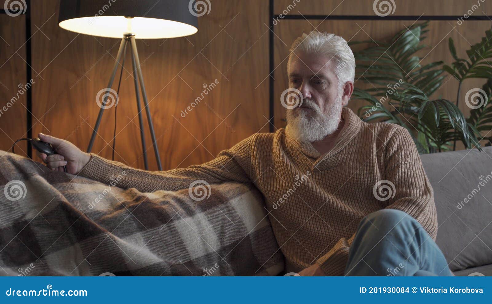 An Elderly Man with a Gray Beard Sitting on the Sofa Turns on and Off ...