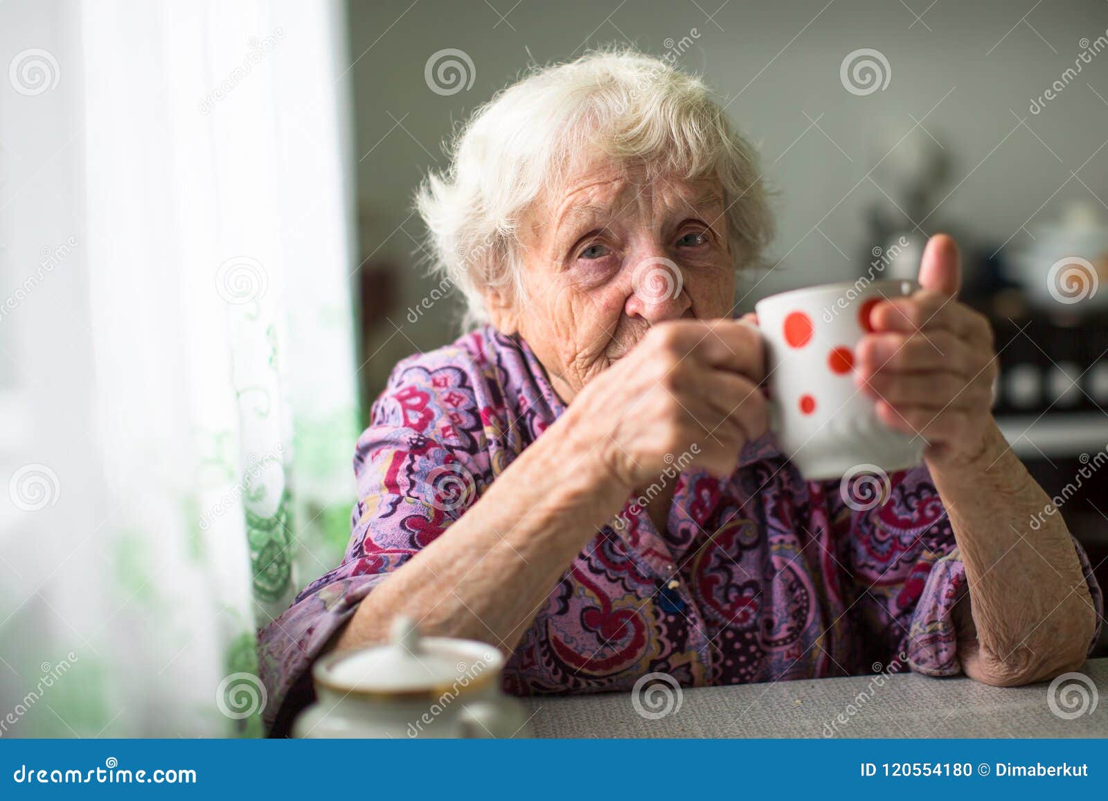 An Elderly Sad Woman Drinks Tea Sitting in the Kitchen. Stock Photo ...