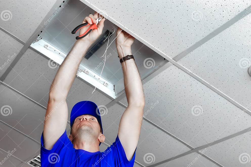 Electrician in Blue Working on Ceiling Wiring, Using Pliers for ...