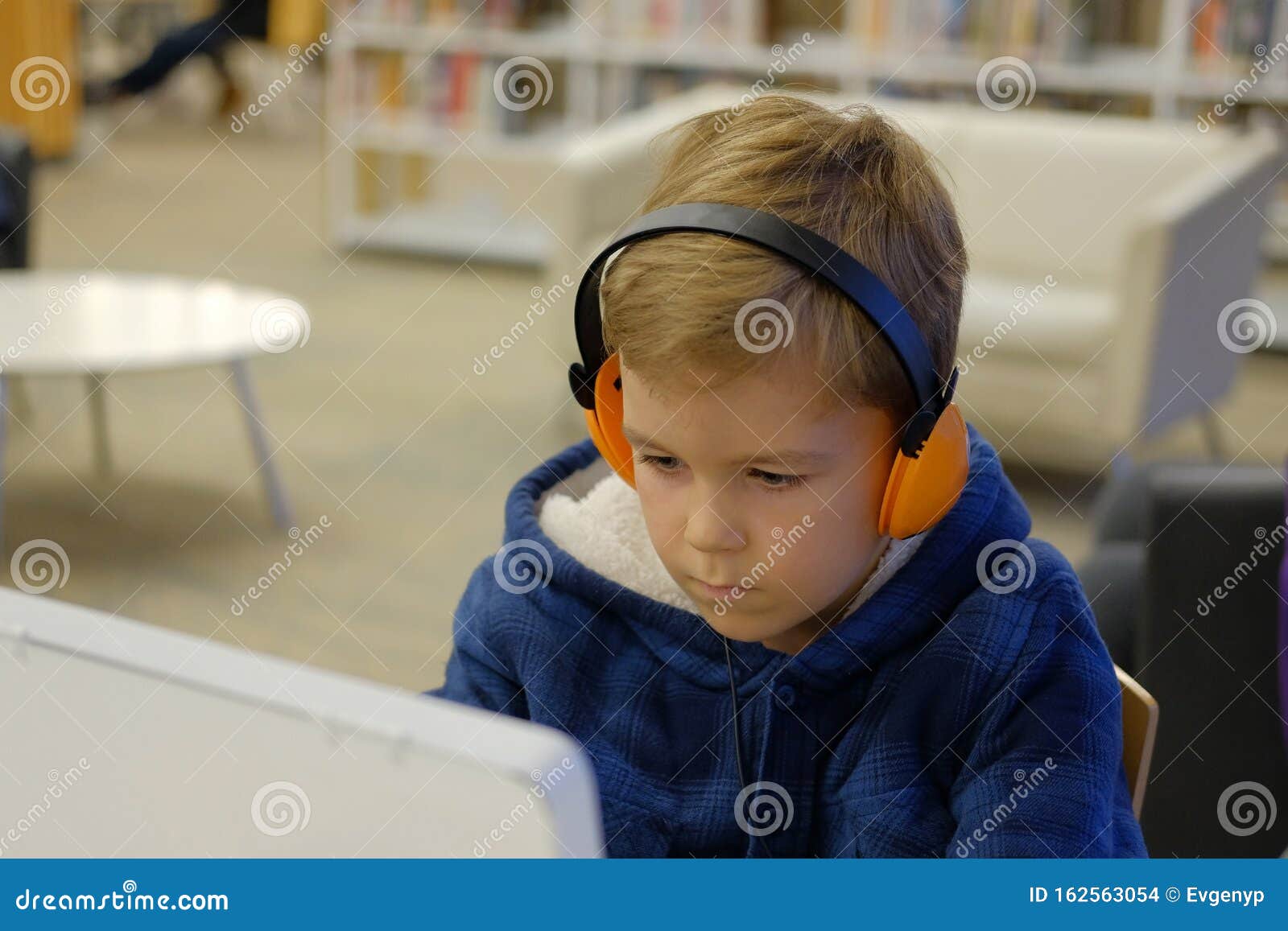 Elementary School Boy Sitting in Library, Using Touchscreen Computer ...