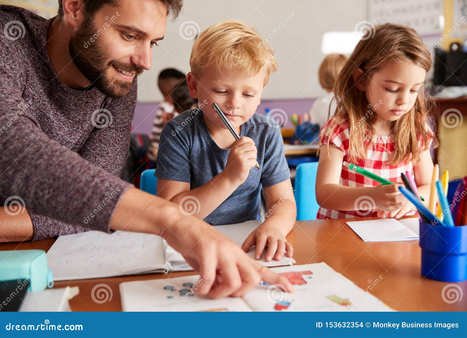 Elementary School Teacher Helping Pupils As they Work at Desk in ...