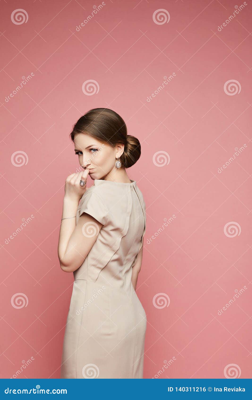 Emotional Brunette Model Girl In A Beige Dress With Stylish Jewelry Isolated At Pink Background