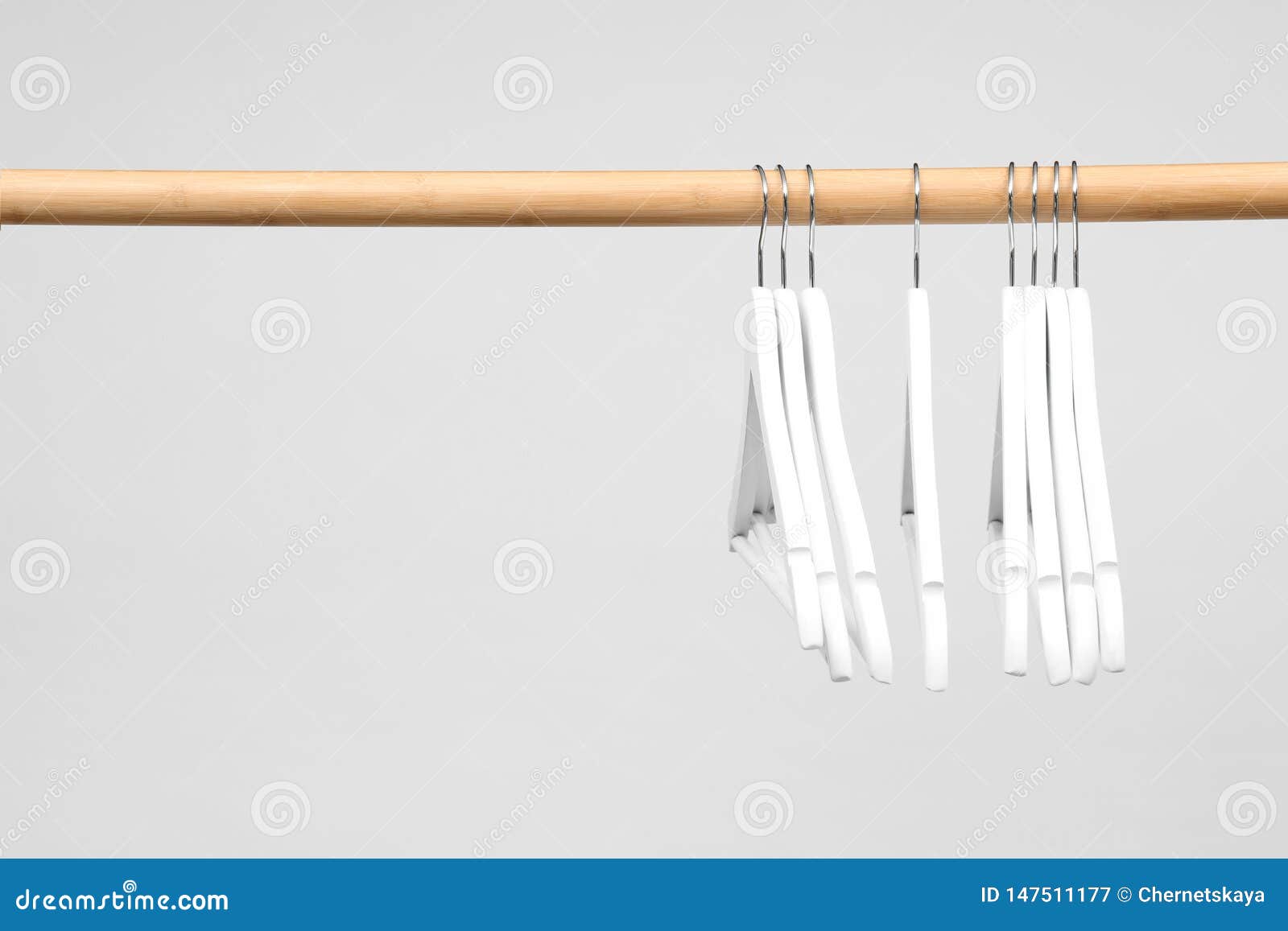 Empty Clothes Hangers on Wooden Rail Against Light Background. Stock ...