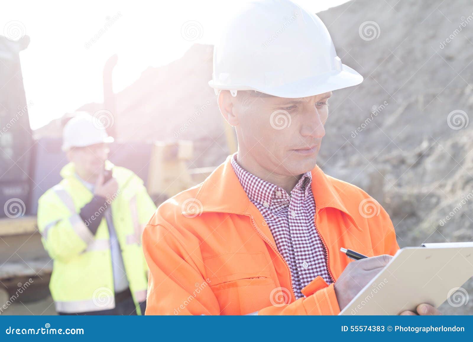 Engineer Writing on Clipboard at Construction Site with Colleague in ...
