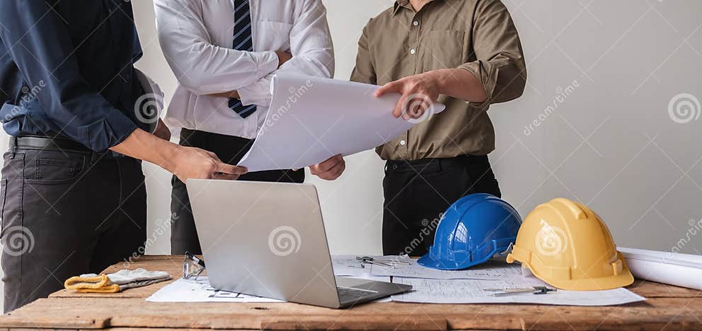 Engineering Team Collaborating on Work Plans at Table with Blueprints ...