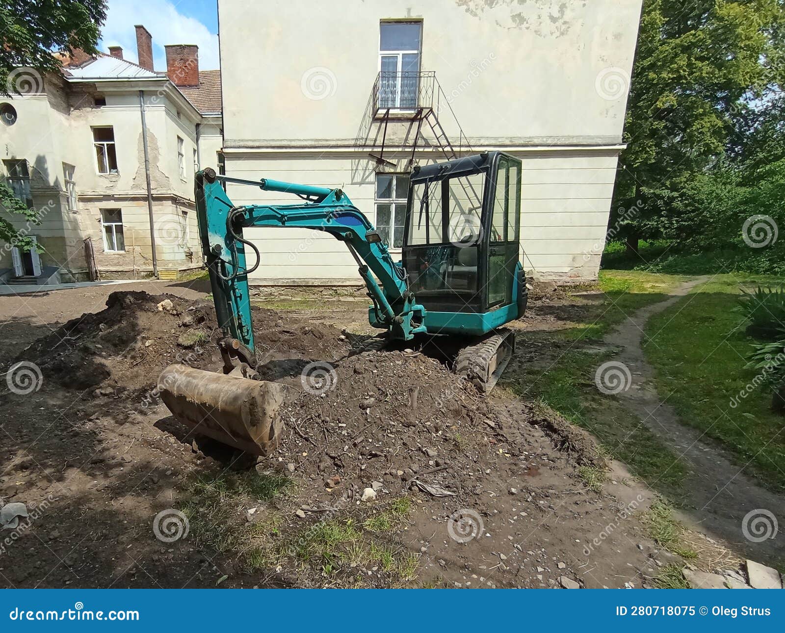 An Excavator is Digging a Hole in the Yard between the Houses Stock ...