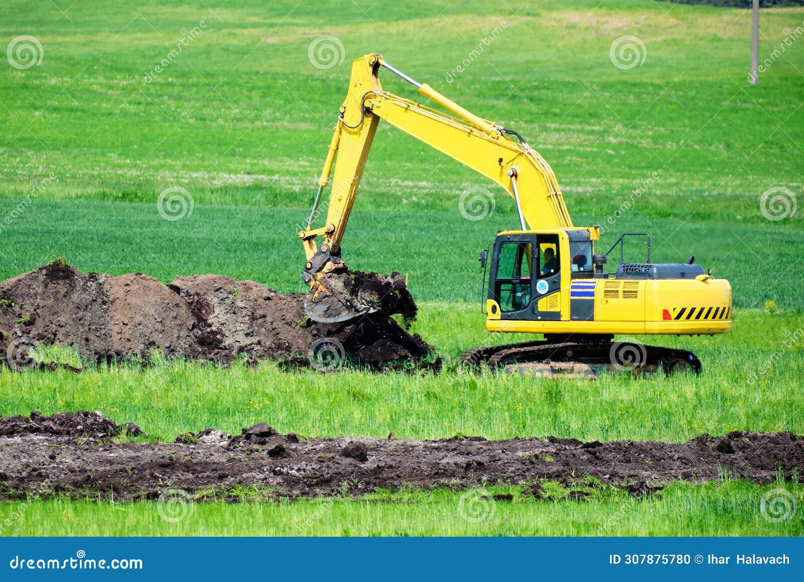 An Excavator while Digging a Trench in a Green Field Stock Photo ...