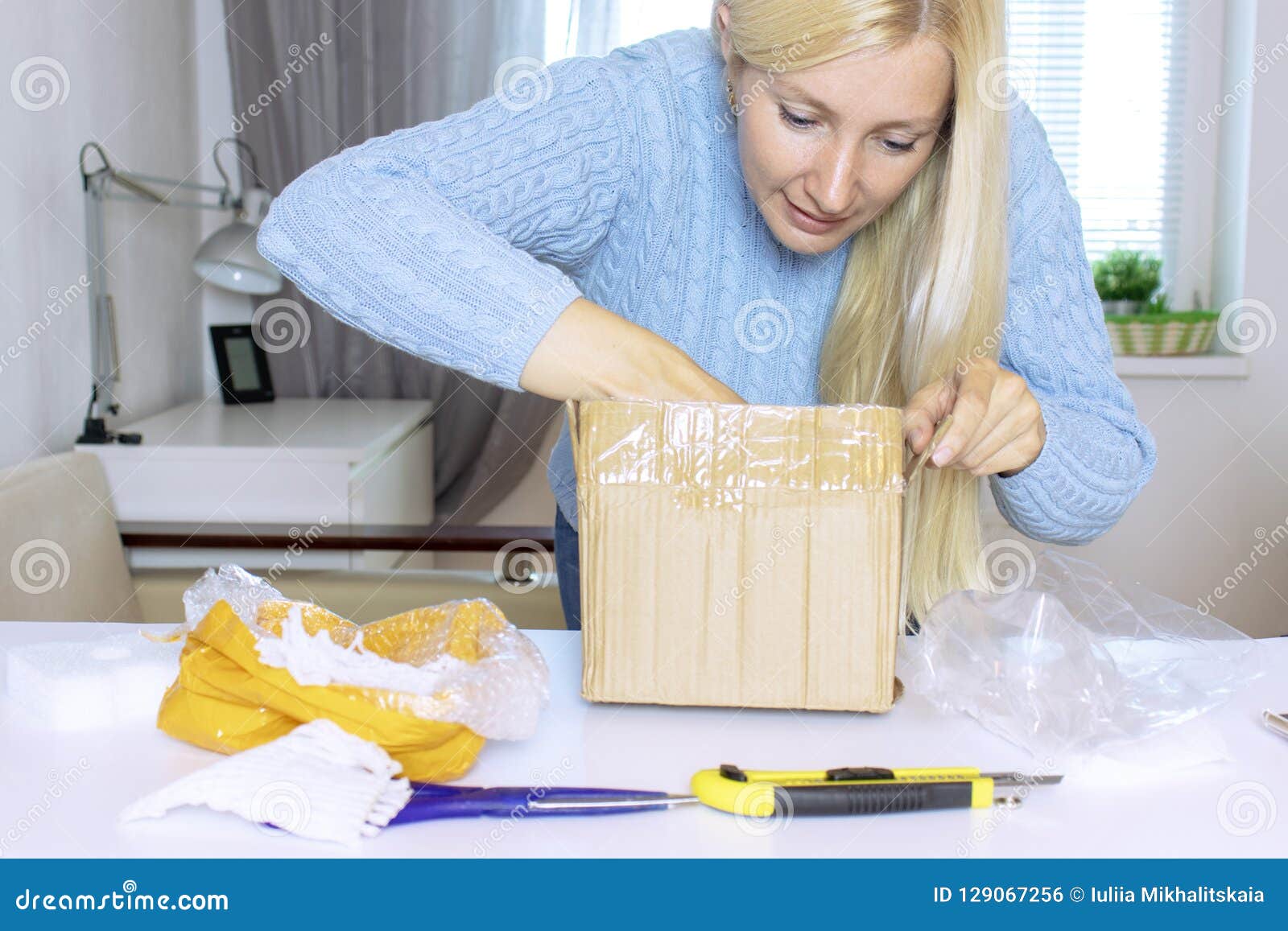 Excited Blond Woman Sitting and Opening a Box, a Parcel, Objects on the ...