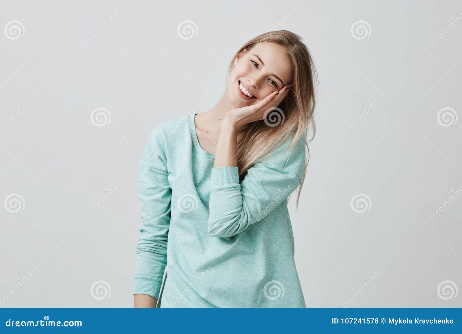 Excited Overjoyed Beautiful Blonde Woman Keeps Hand On Cheek Smiles