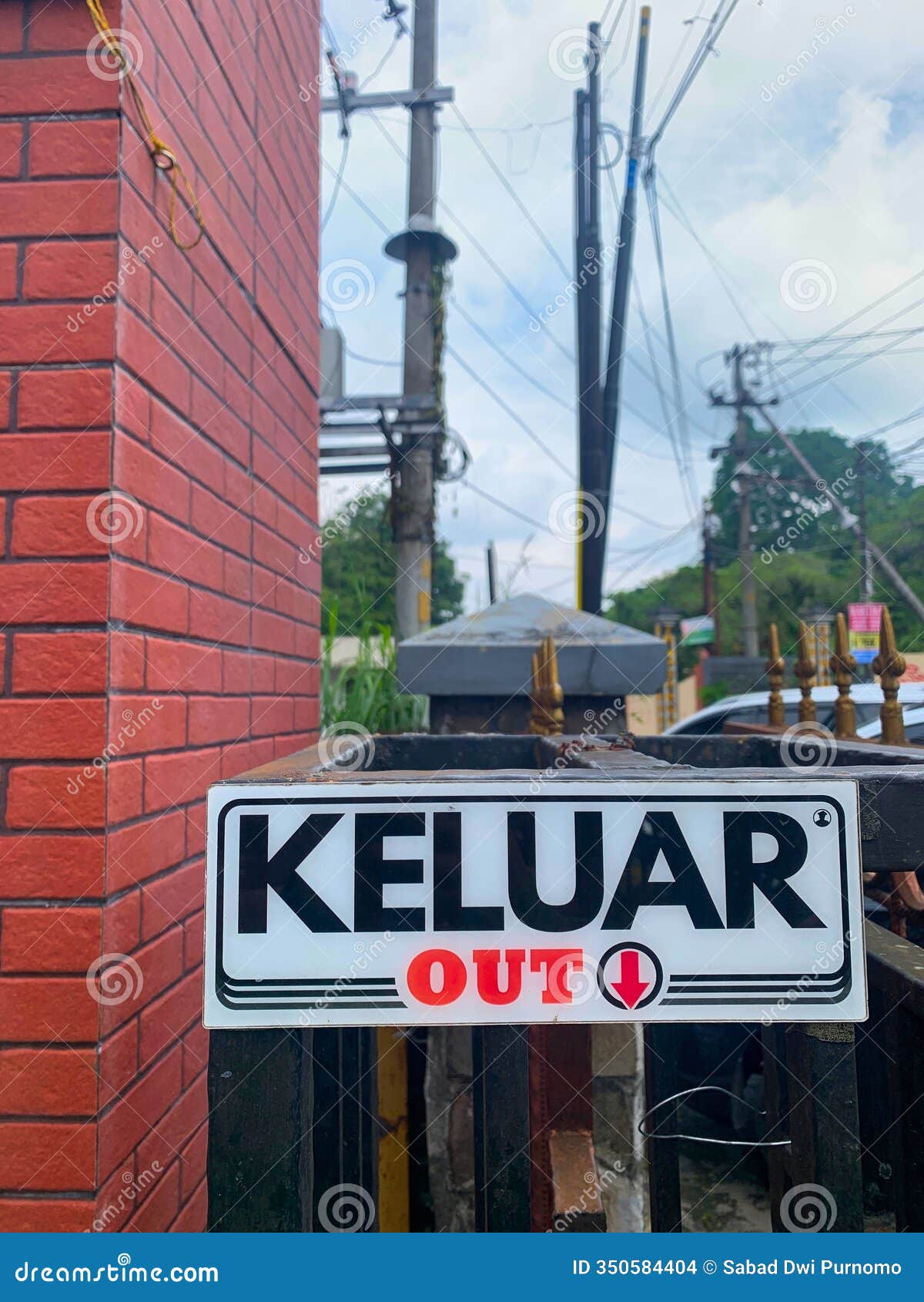 Exit Sign Keluar (Out) on Fence with Red Brick Wall and Utility Poles ...