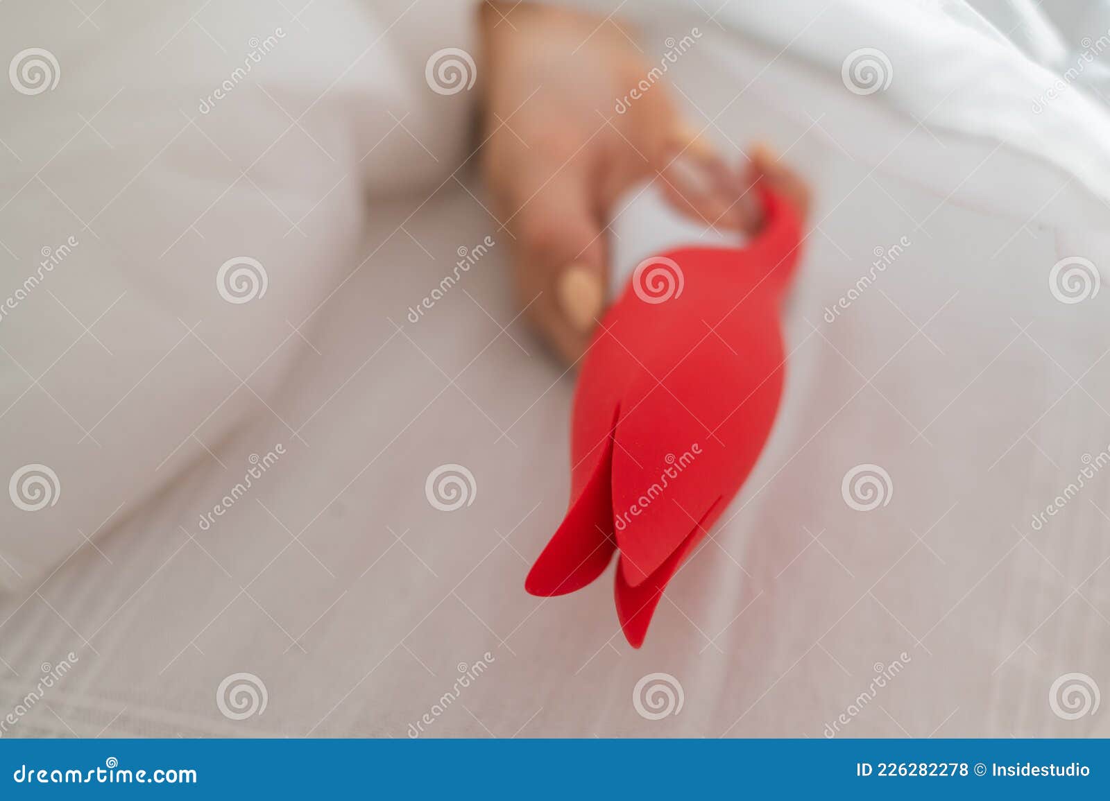 A Faceless Woman Lies In Bed Under A Blanket Holding A Clitoral