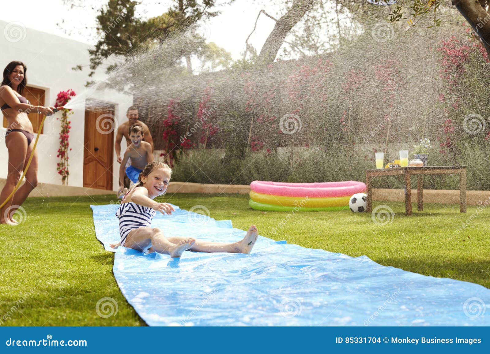 Family Having Fun on Water Slide in Garden Stock Photo - Image of ...