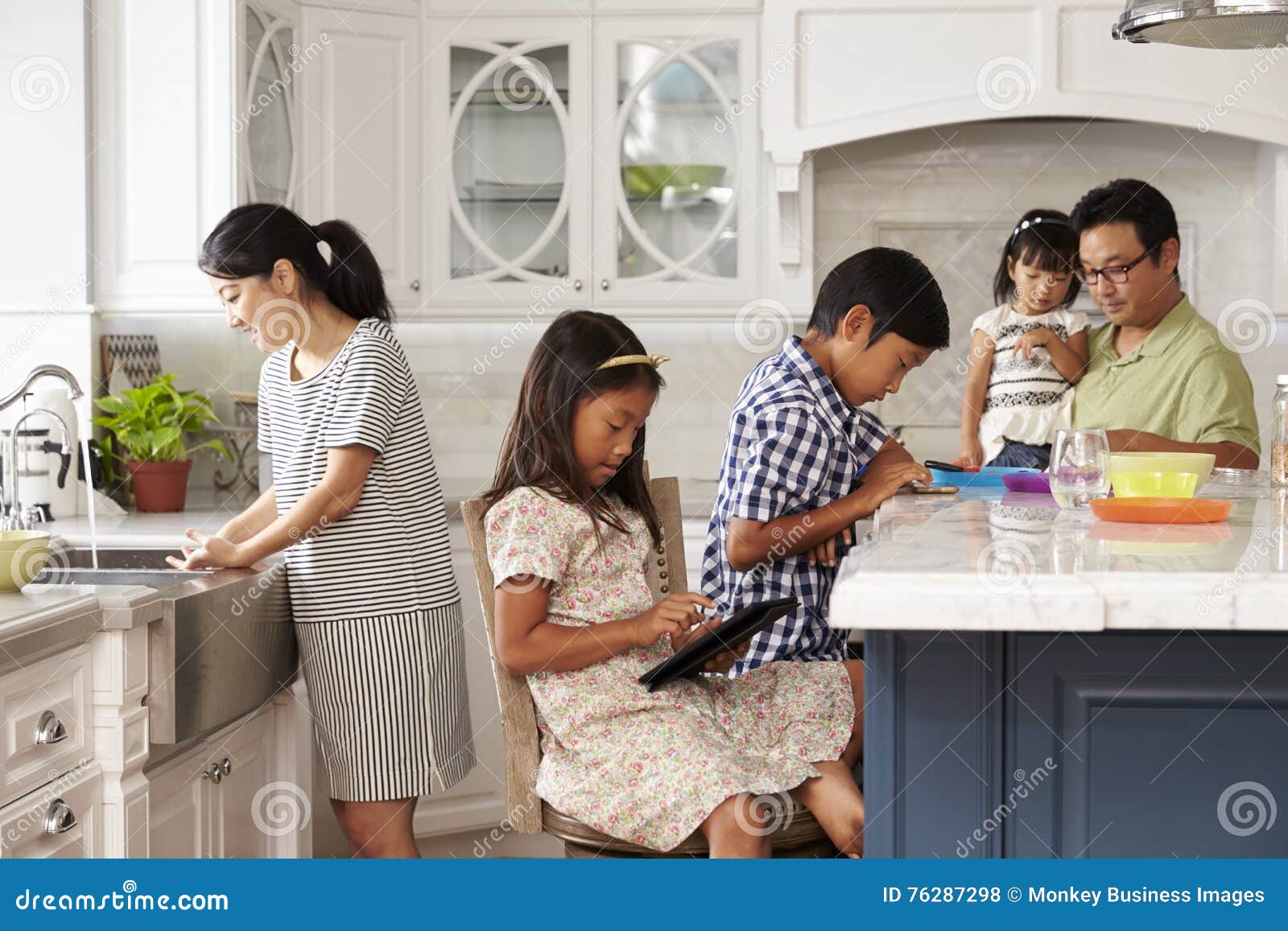 Family in Kitchen Doing Chores and Using Digital Devices Stock Photo ...
