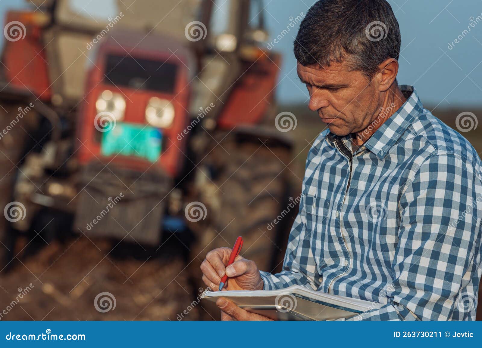 Farmer Writing Notes in Front of Tractor in Field Stock Image - Image ...