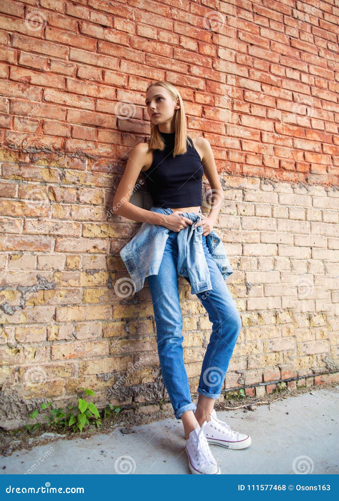 Fashion Girl Standing Near Brick Wall In Denim And Sneakers Vogue