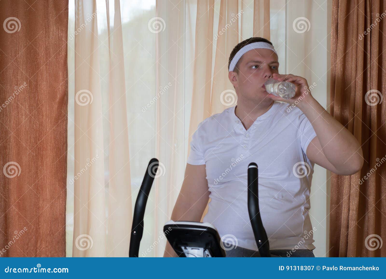 Fat Guy Exercising on Stationary Training Bicycle and Drinking Water ...