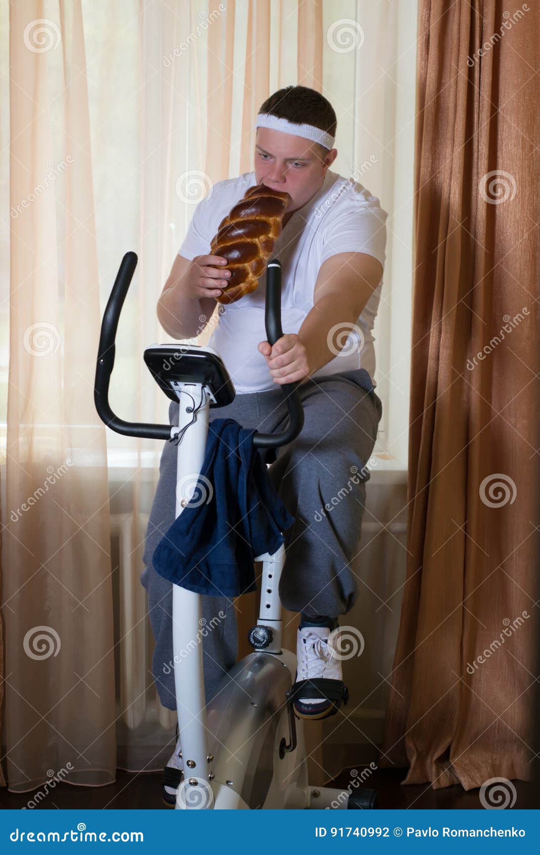 Fat Guy Exercising on Stationary Training Bicycle and Eating a Bun ...