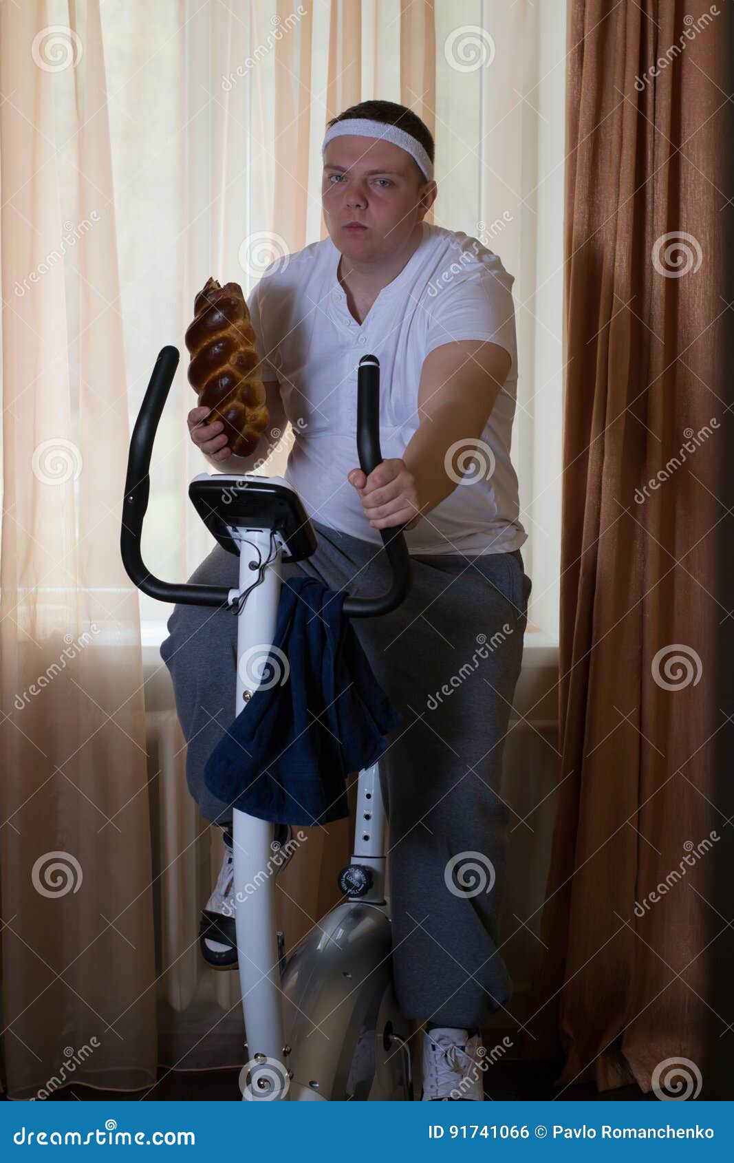 Fat Guy Exercising on Stationary Training Bicycle and Eating a Bun ...