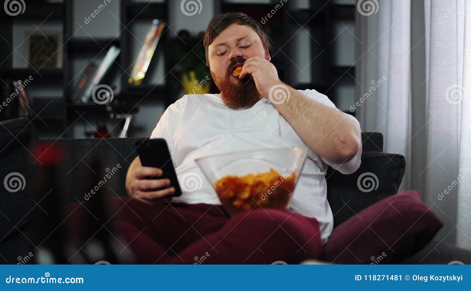 Fat Man Smiles while he Reads Something in His Smartphone and Eats ...
