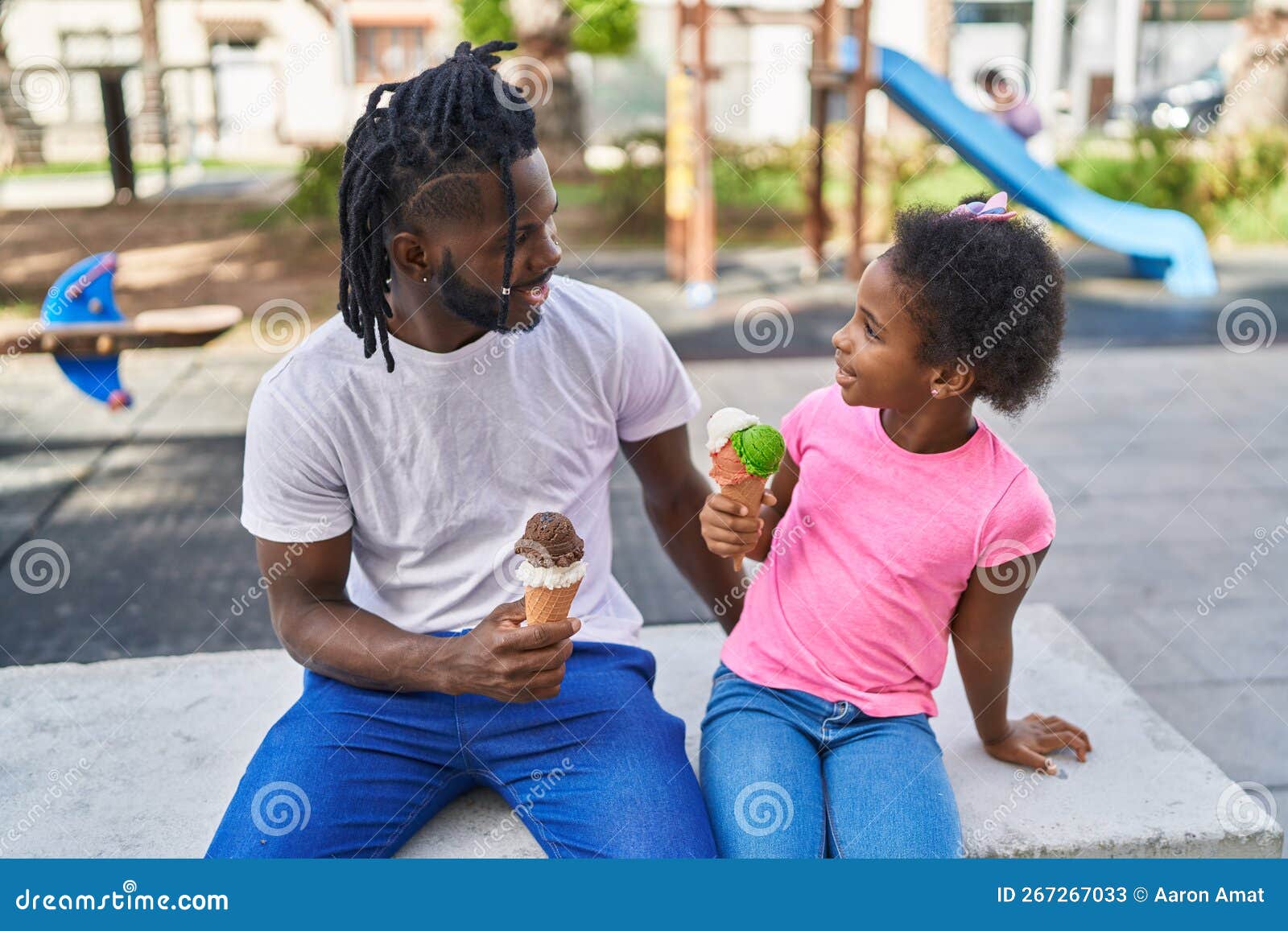 Father And Daughter Eating Ice Cream Sitting Together On Bench At Park