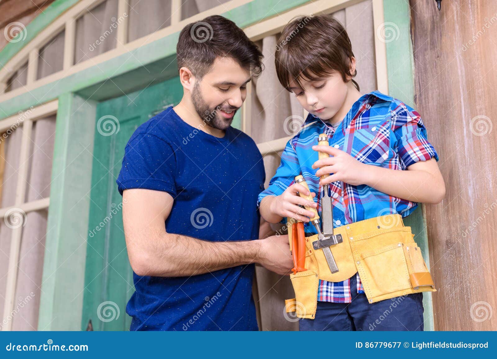 Father Looking at Son Standing in Tool Belt and Holding Tools Stock ...