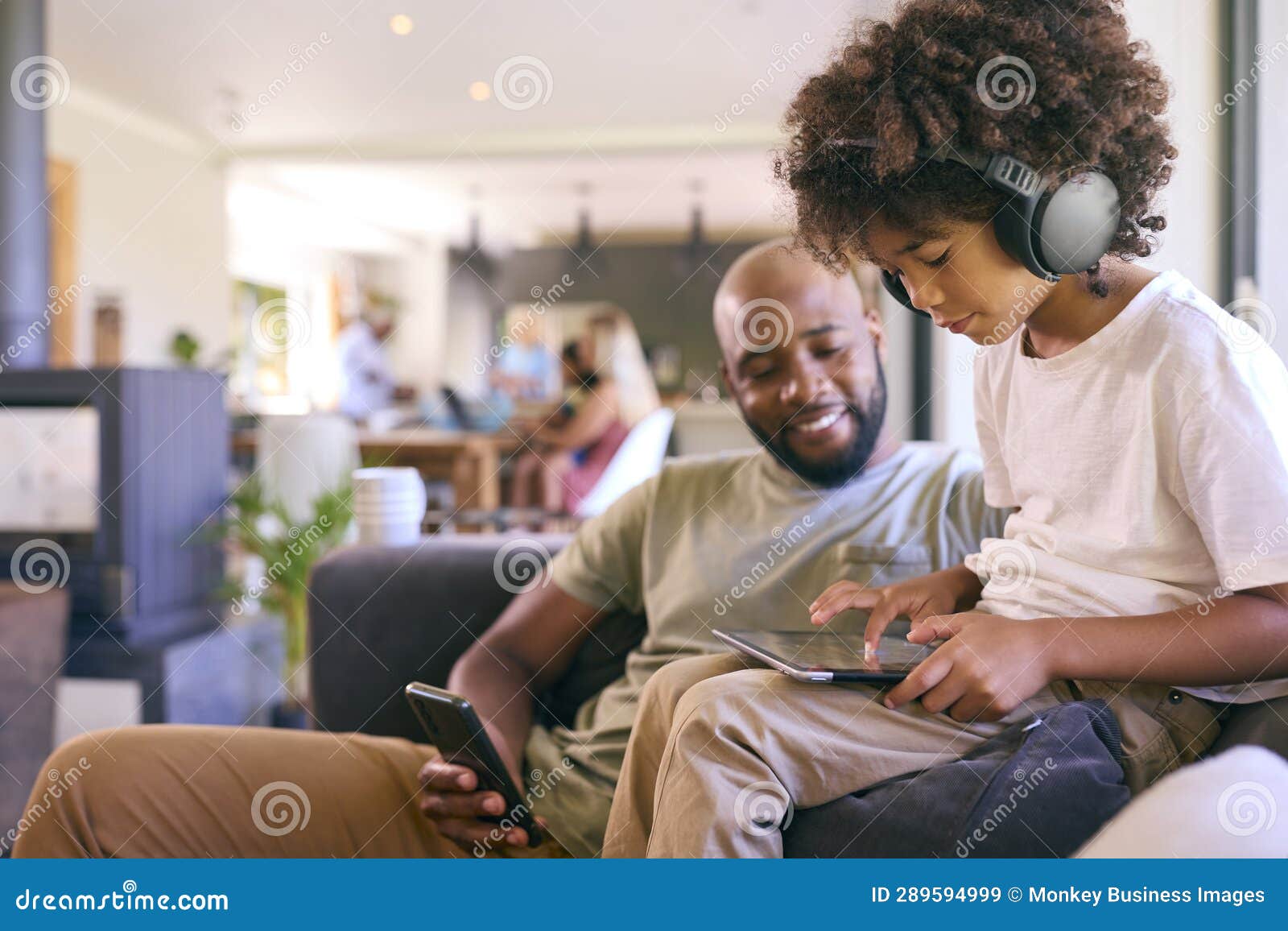 Father with Mobile Phone and Son Using Digital Tablet with Headphones ...