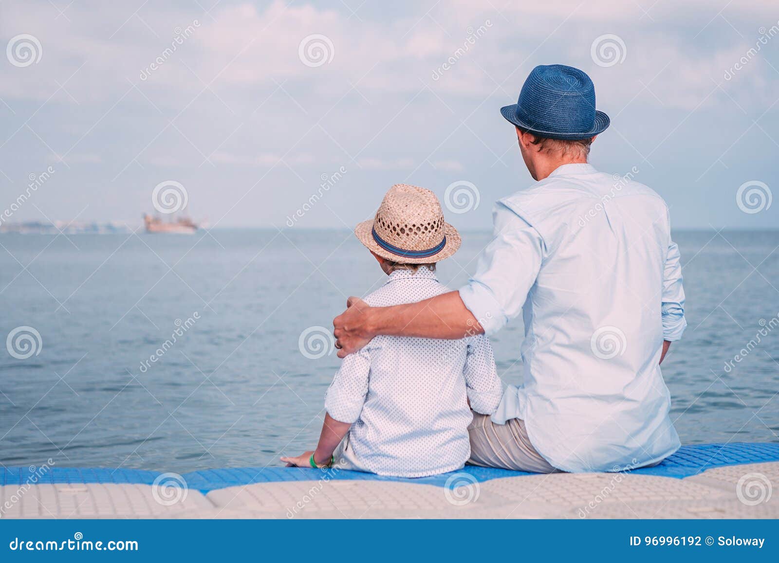 Father and Son Sit on the Sea Pier and Look on the Ship on Horizont ...