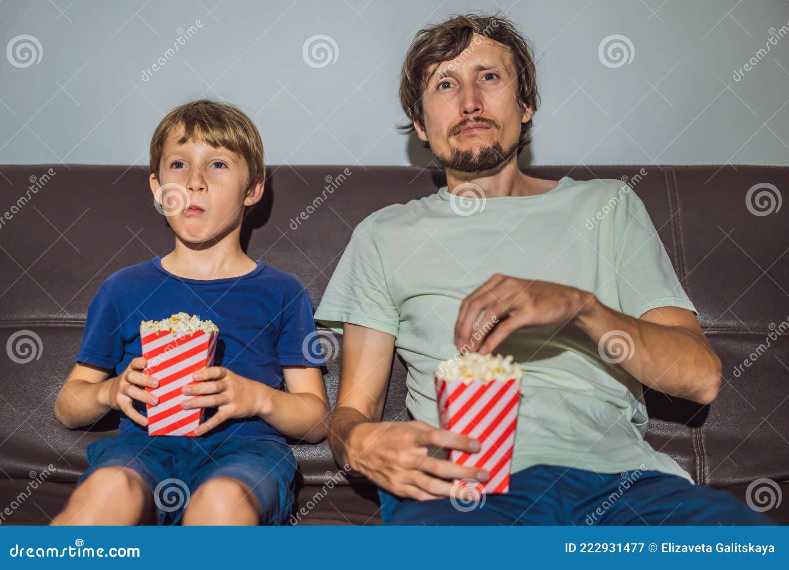 Father And Son Watching Tv And Eat Popcort In Evening At Home Stock