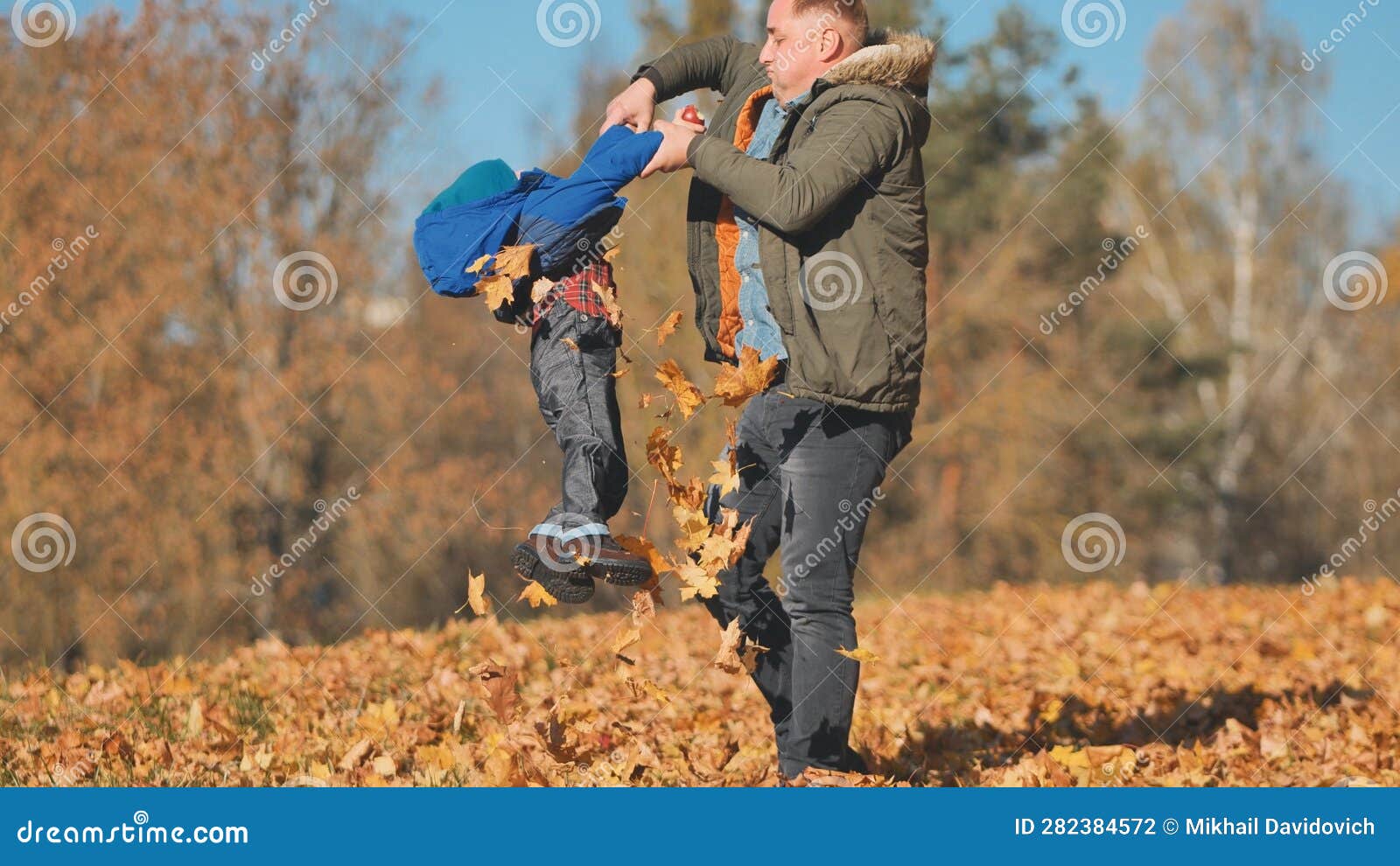 A Father Spins His Son by His Feet in the Park in the Fall. Stock Photo ... A Father Spins His Son by His Feet in the Park in the Fall. Stock Photo ...