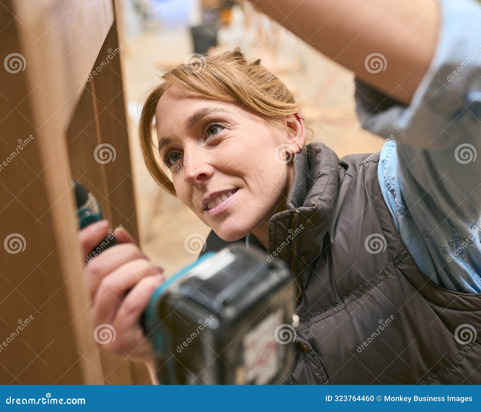 Female Carpenter In Workshop Using Drill To Attach Piece Of Wood To ...