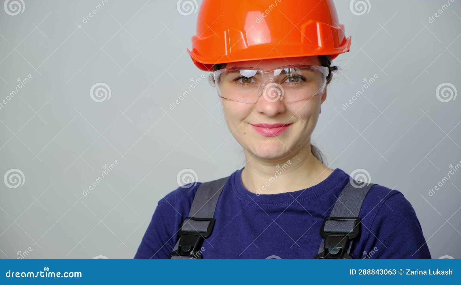 A Female Engineer in Work Overalls and a Helmet Wears Goggles on a ...