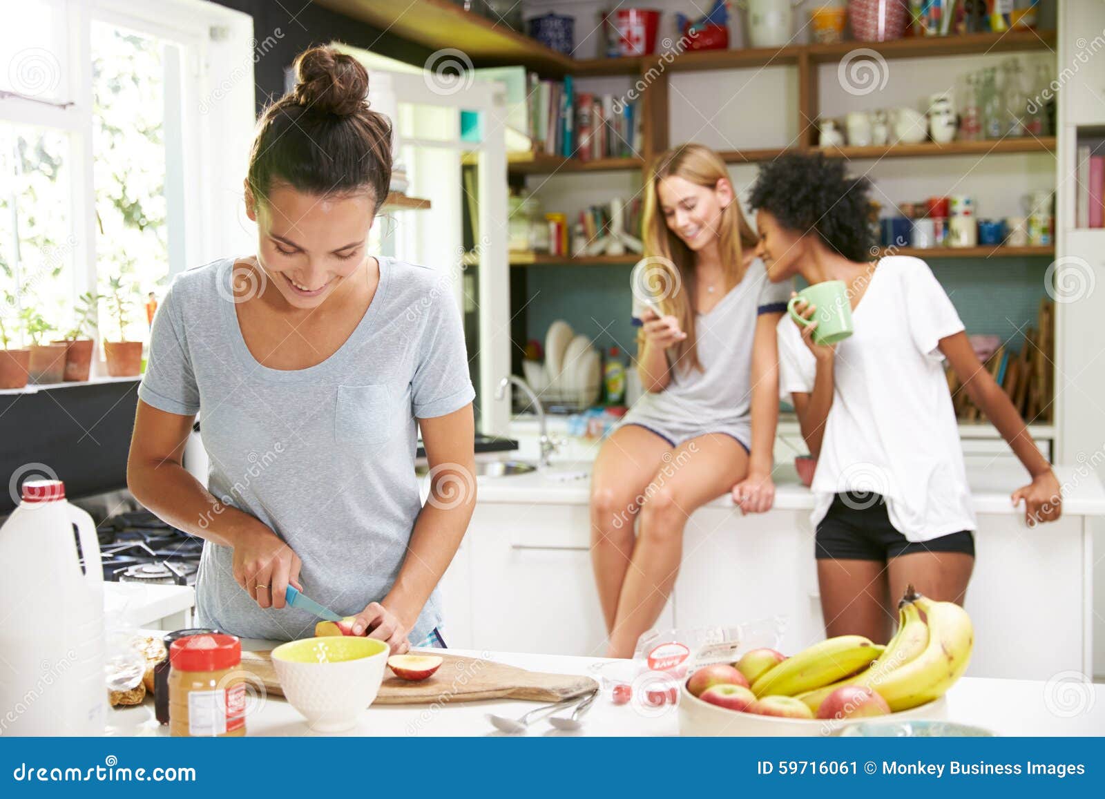 Female Friends Making Breakfast Whilst Checking Mobile Phone Stock ...