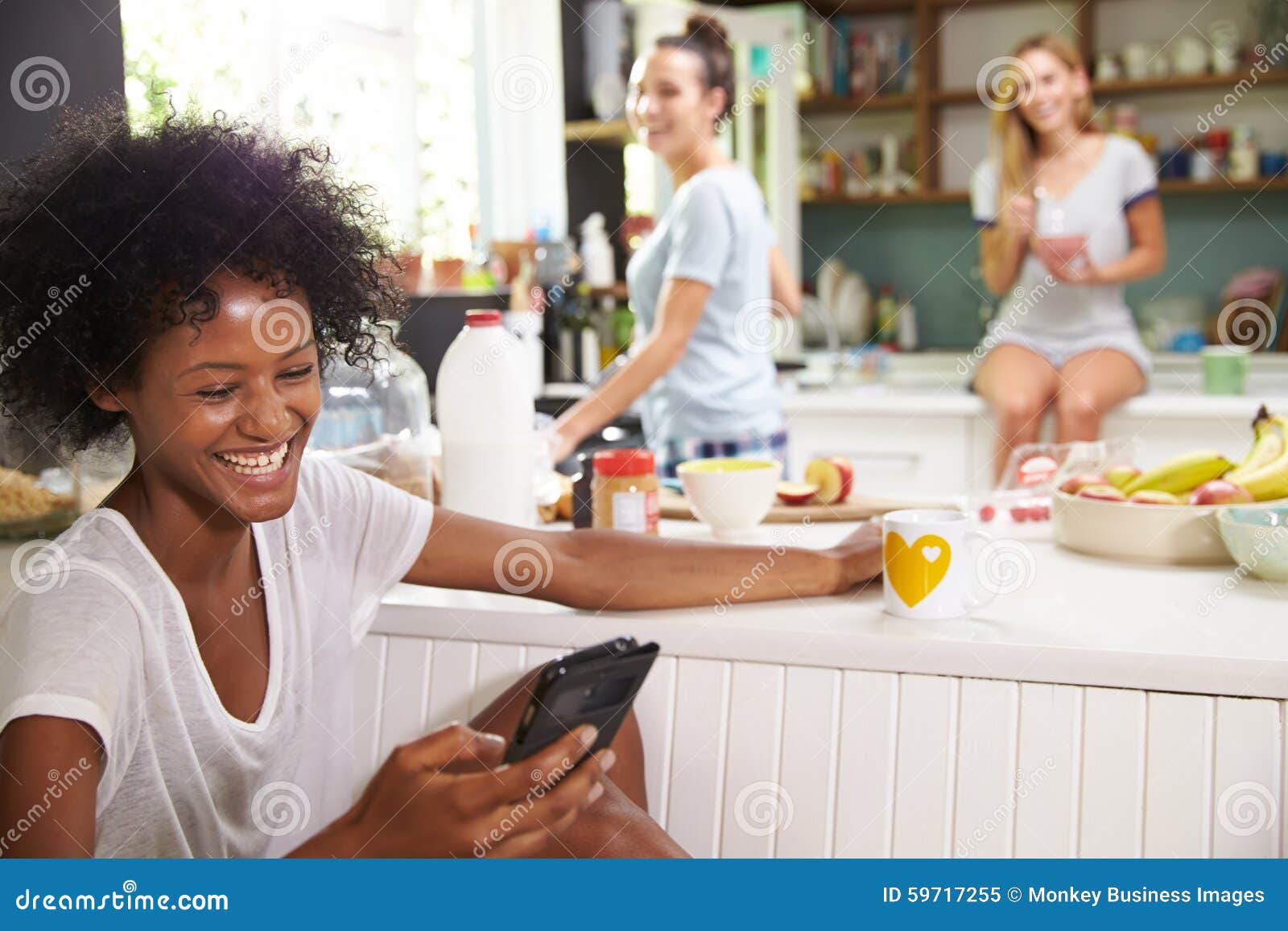 Female Friends Making Breakfast Whilst Checking Mobile Phone Stock ...