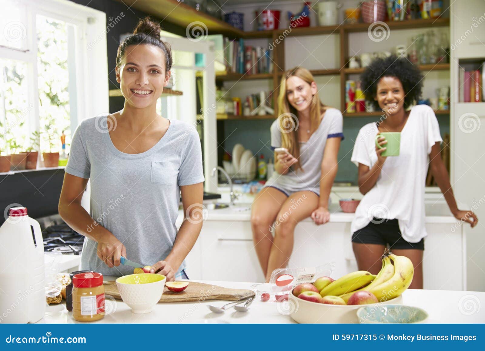 Female Friends Making Breakfast Whilst Checking Mobile Phone Stock ...