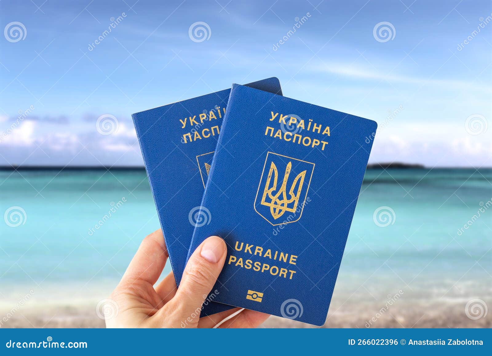 Female Hand Holds Two Ukrainian Passports Against The Ocean In The