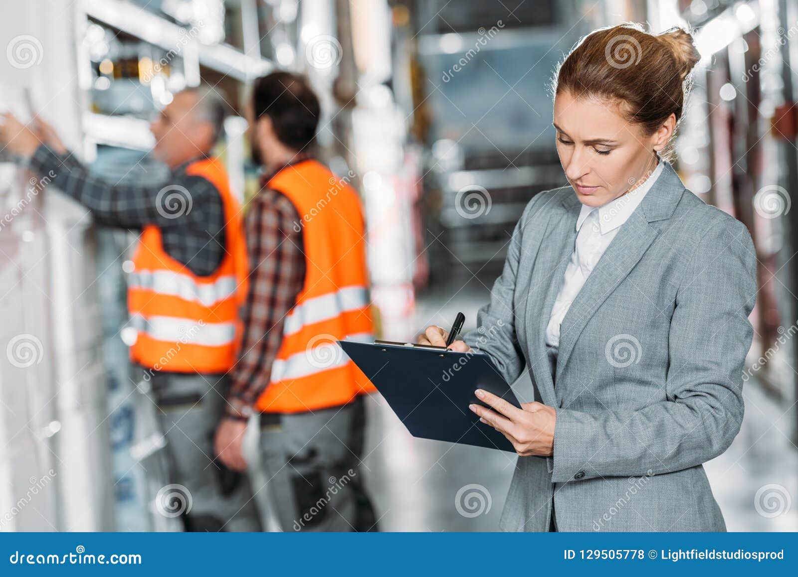 Female Inspector Writing Something while Men Working Behind Stock Photo ...