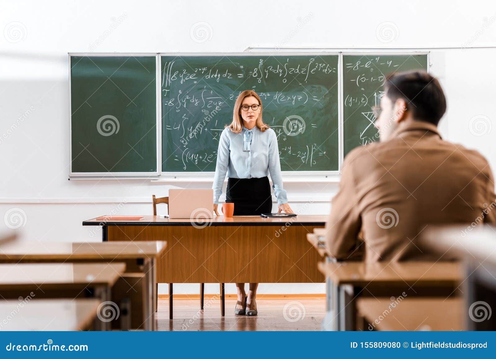 Female Lecturer Standing at Desk Near Chalkboard with Equations Stock ...