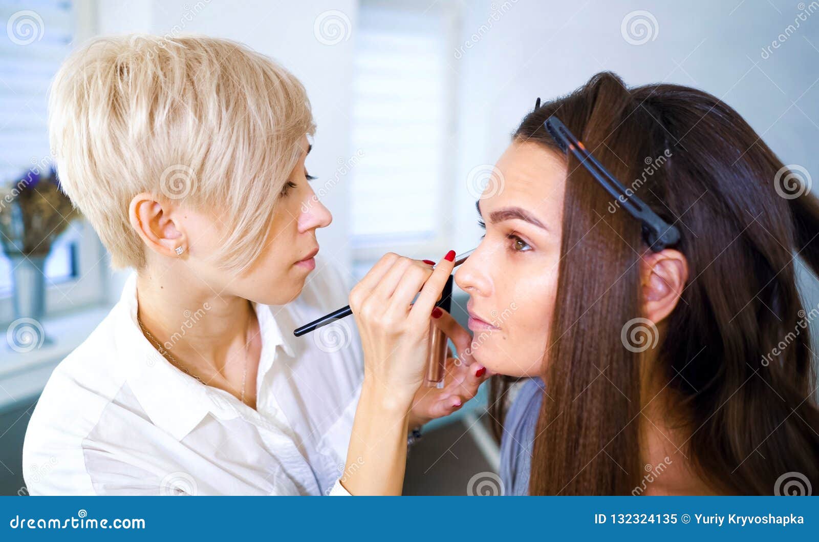 Female Makeup Artist Doing Professional Makeup For Young Brunette Woman