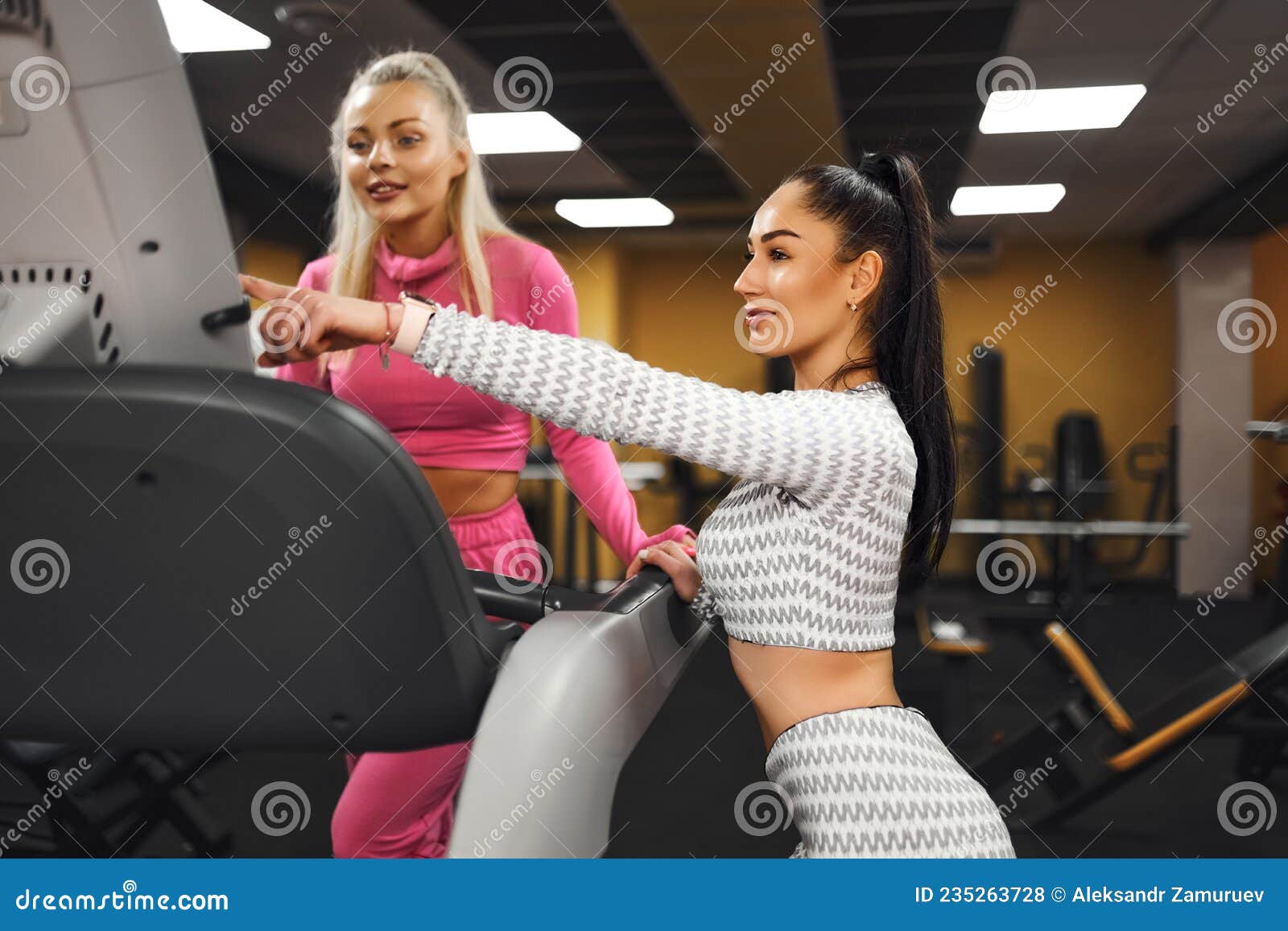 Female Personal Trainer Helping Woman Client Use Treadmill In Gym