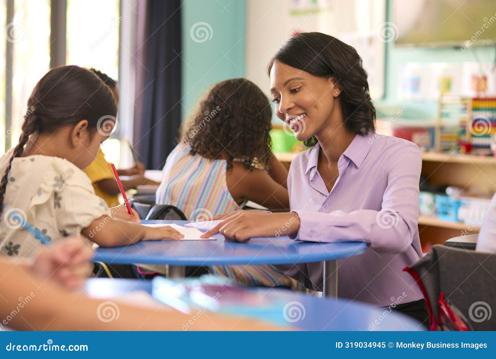 Female Primary or Elementary School Teacher Helping Students at Desks ...