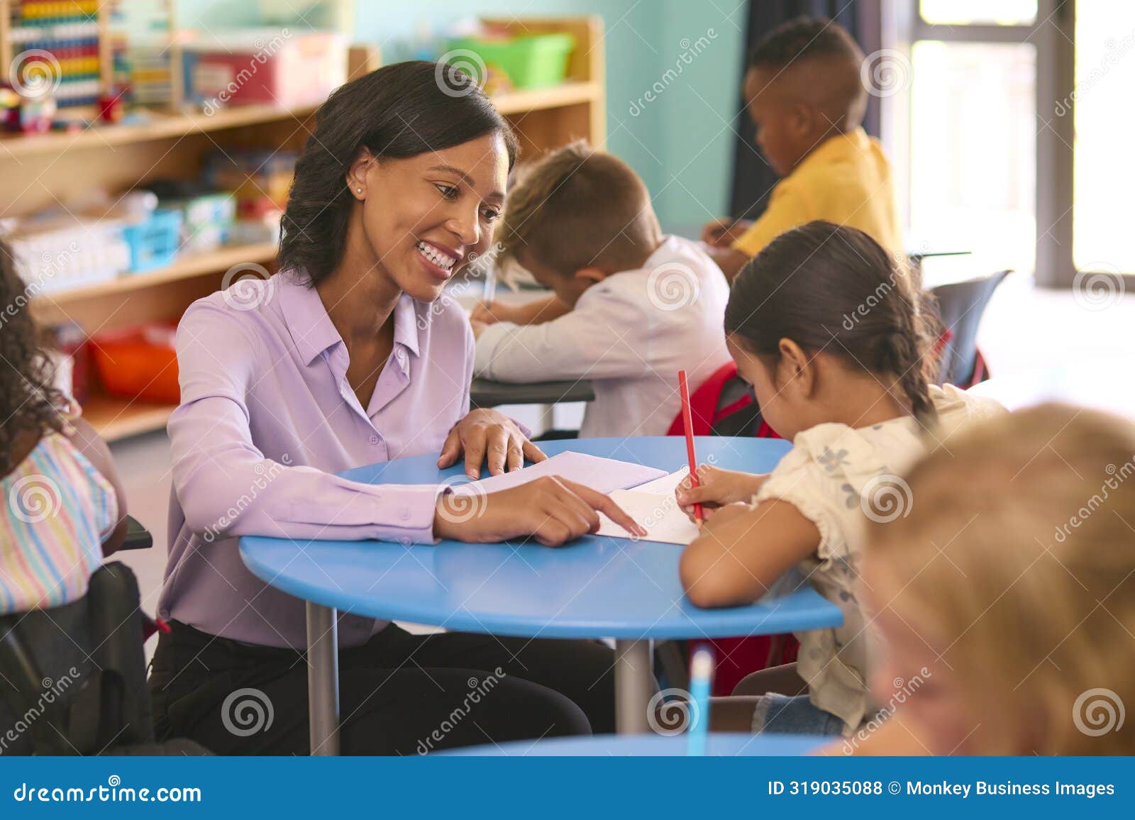 Female Primary or Elementary School Teacher Helping Students at Desks ...