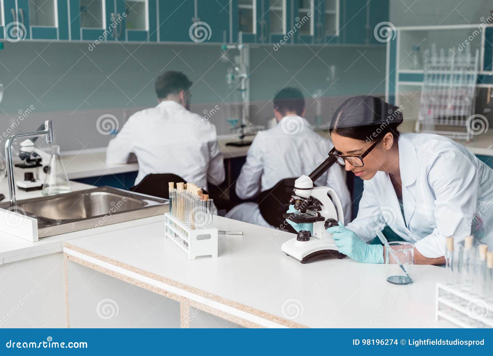 Female Scientist in Eyeglasses Working with Microscope while Colleagues ...