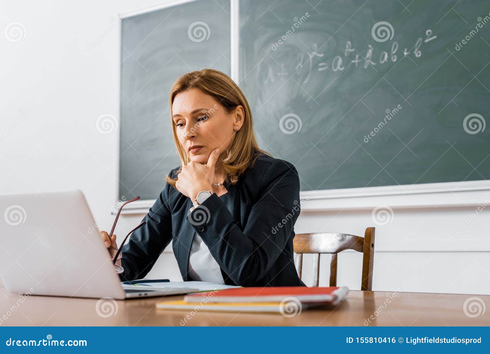 Female Teacher Sitting at Desk and Using Computer during Lesson Stock ...