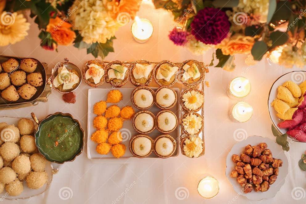 A Festive Table Setting with Various Indian Sweets, Snacks, and Candles ...