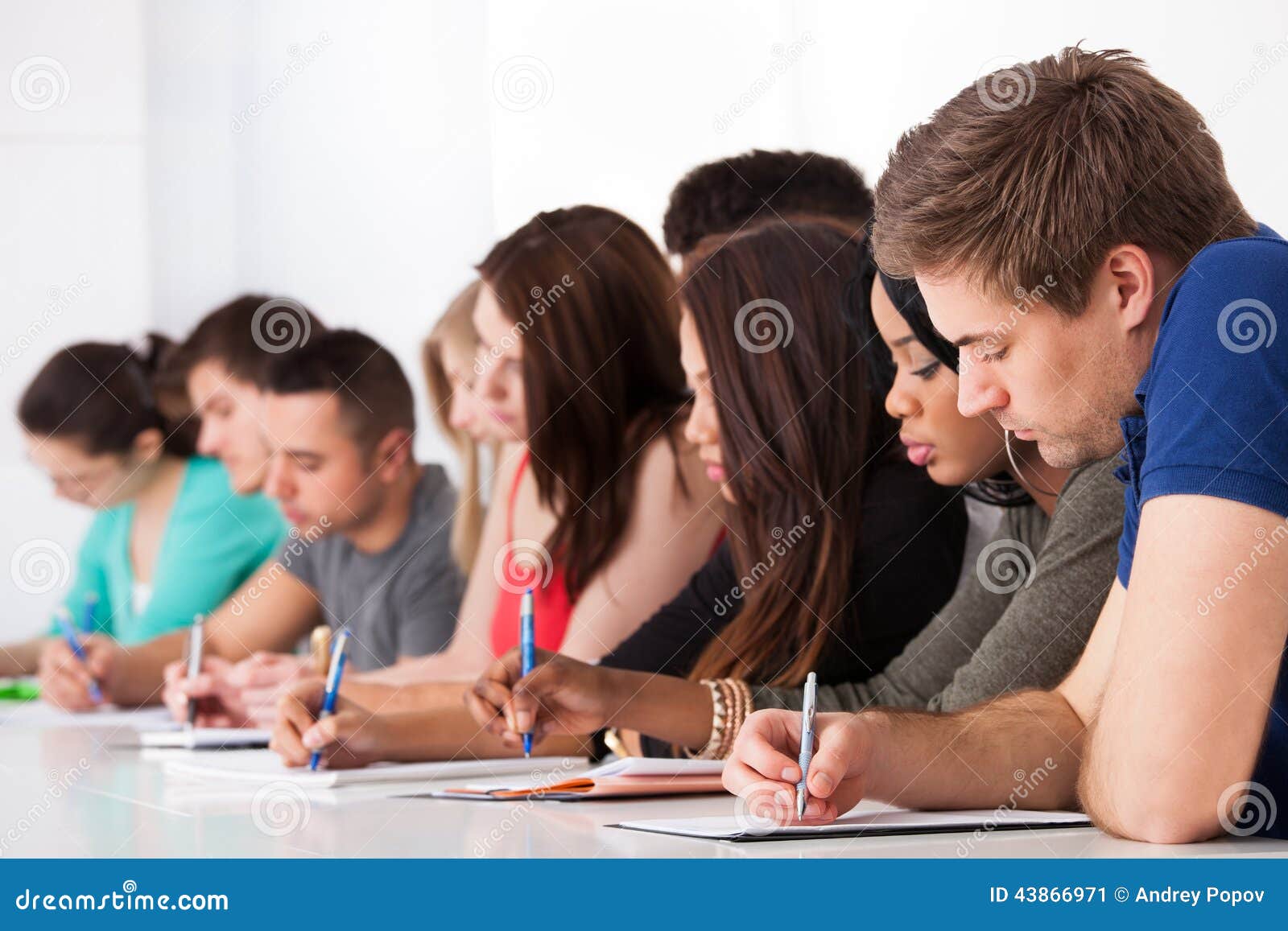 Fila De Los Estudiantes Universitarios Que Escriben En El Escritorio ... Fila De Los Estudiantes Universitarios Que Escriben En El Escritorio ...