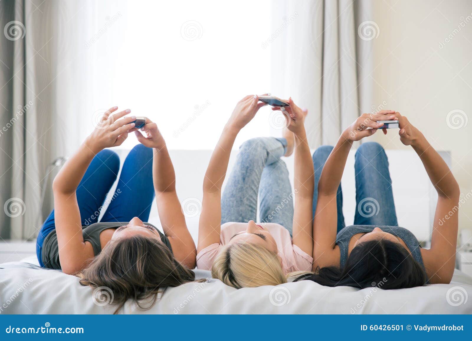 Filles Se Trouvant Sur Le Lit Et à Laide Des Smartphones Image Stock