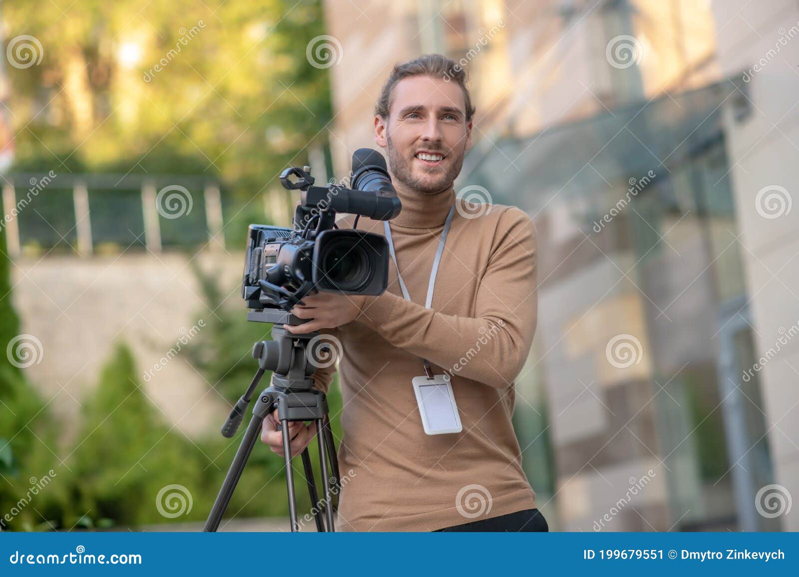 Smiling Fair-haired Cameraman Carring Camera with Tripod Outside Stock ...