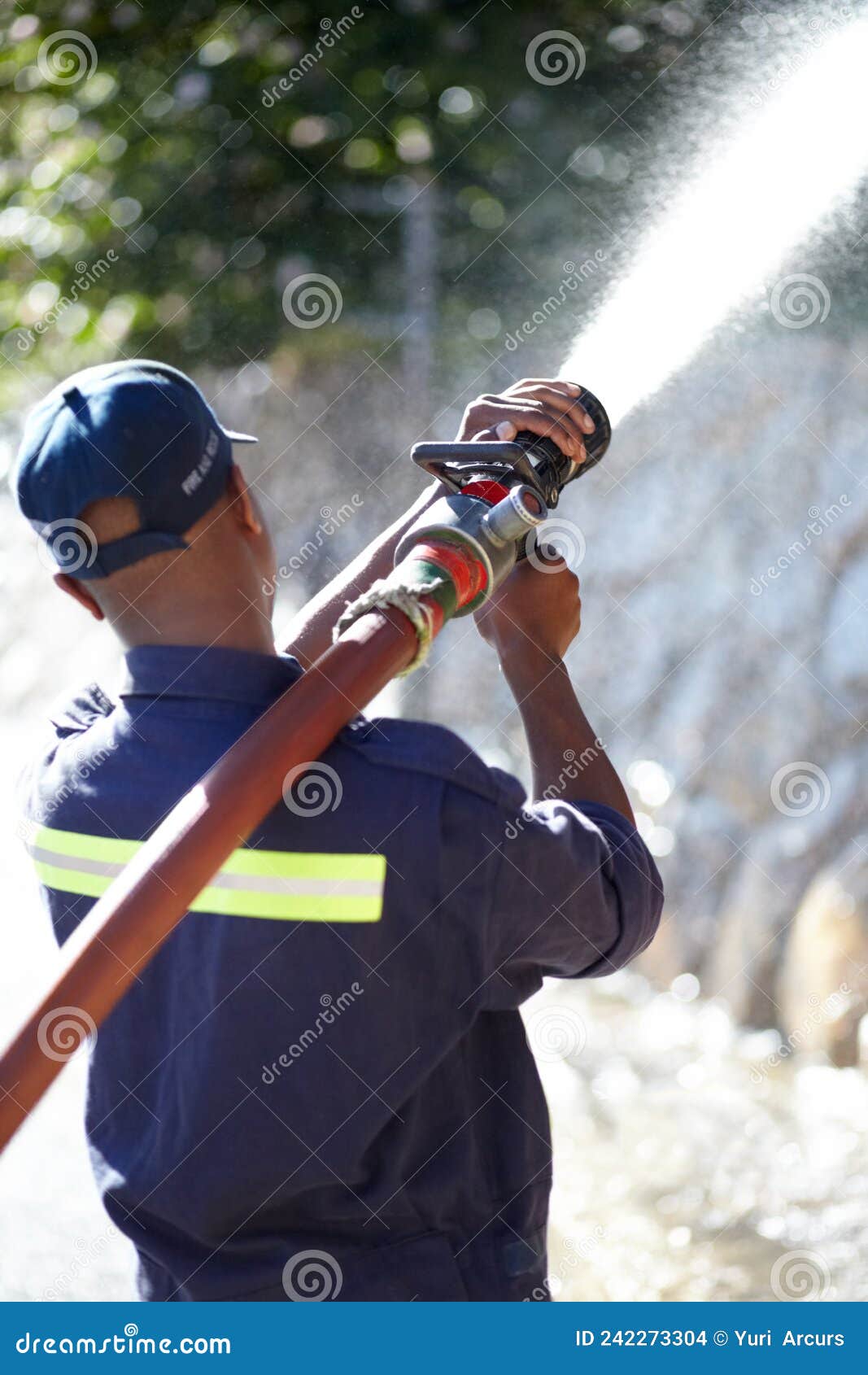 Fireman at Work. Rearview Shot of a Fireman Spraying Water with a Fire ...
